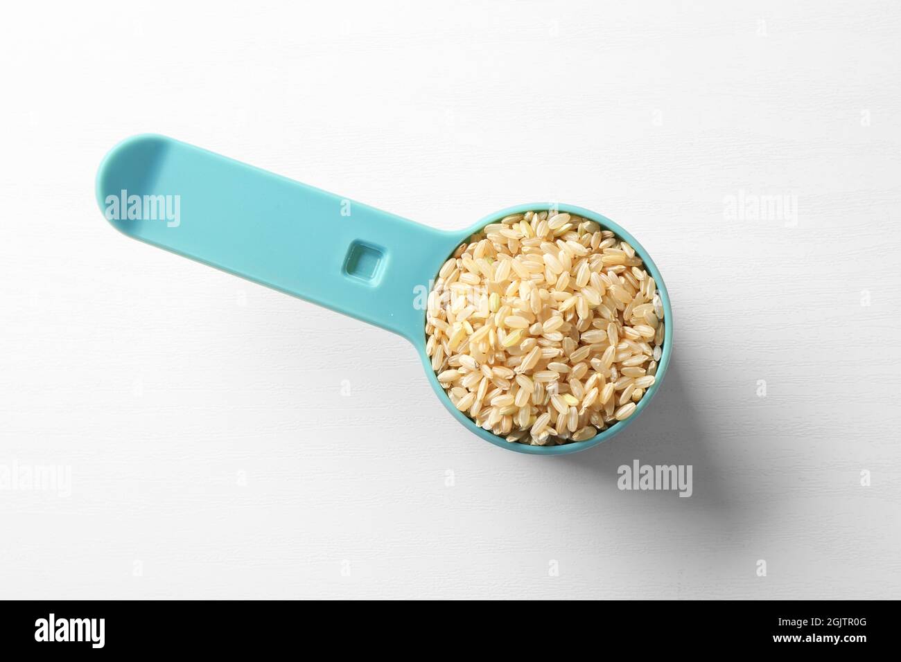 Measure scoop full of brown rice on white background Stock Photo - Alamy