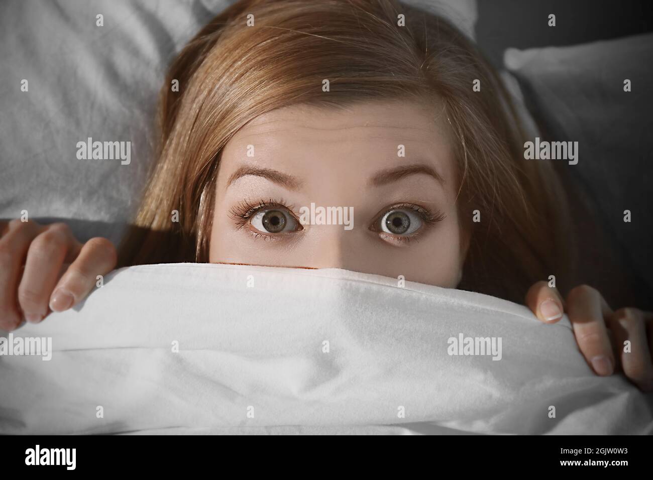 Young scared woman hiding under blanket while lying in bed at home ...