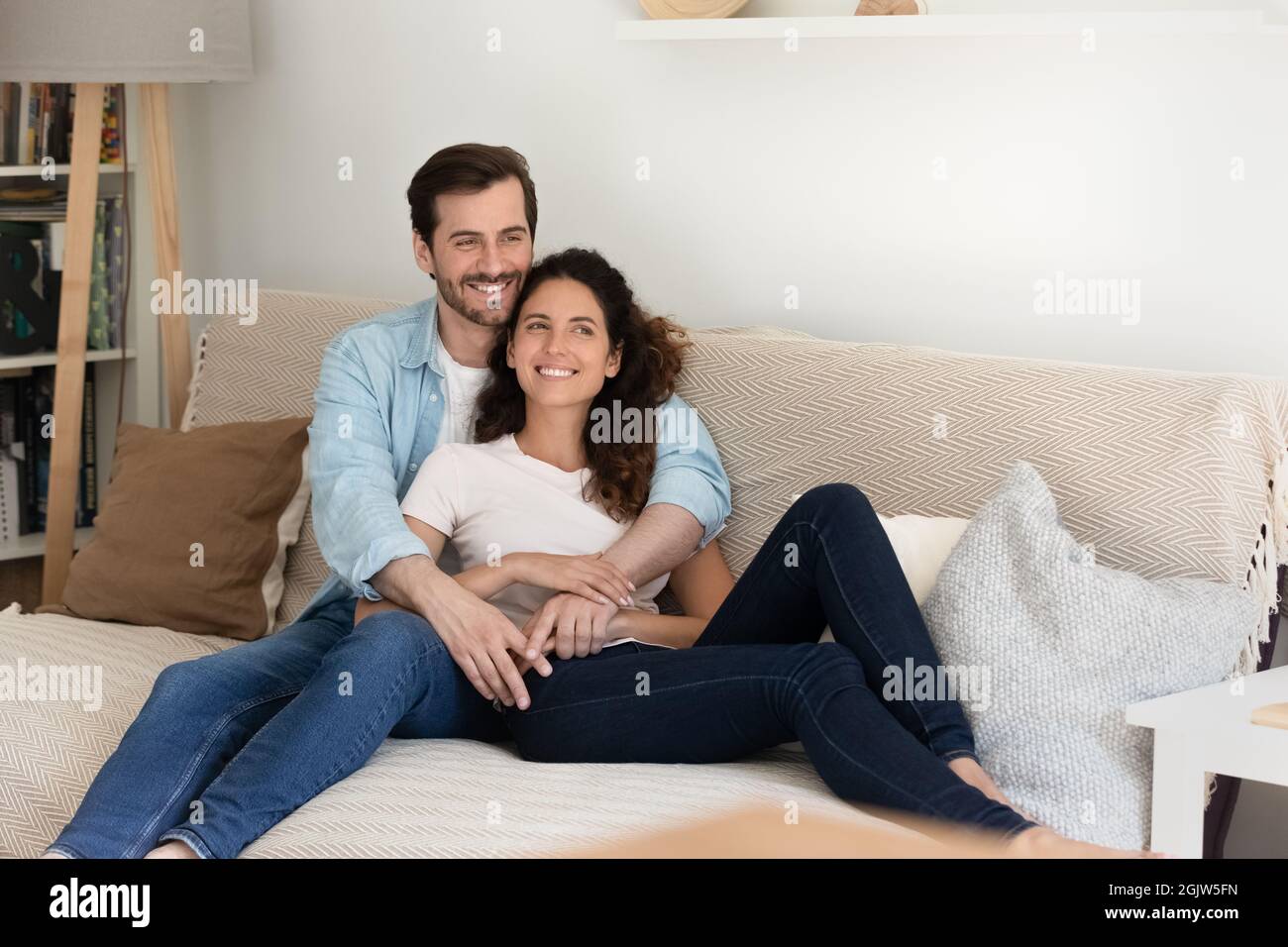 Couple hugging resting at home smiling daydreaming looking into ...