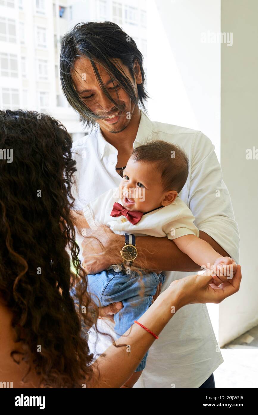 Happy parents playing with smiling baby boy wearing pants, shirt and ...