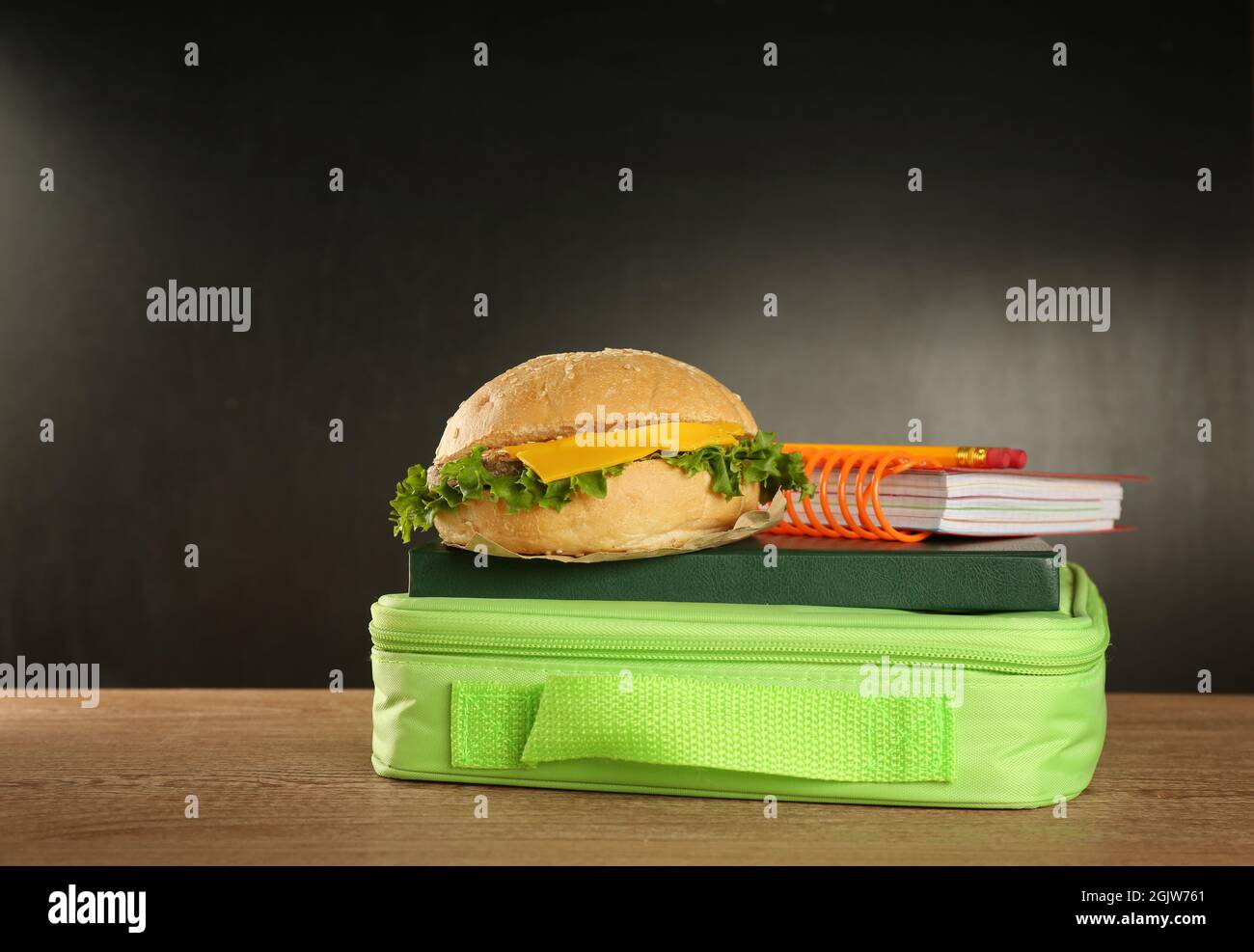 Modern lunch box with hamburger and exercise books on wooden table ...