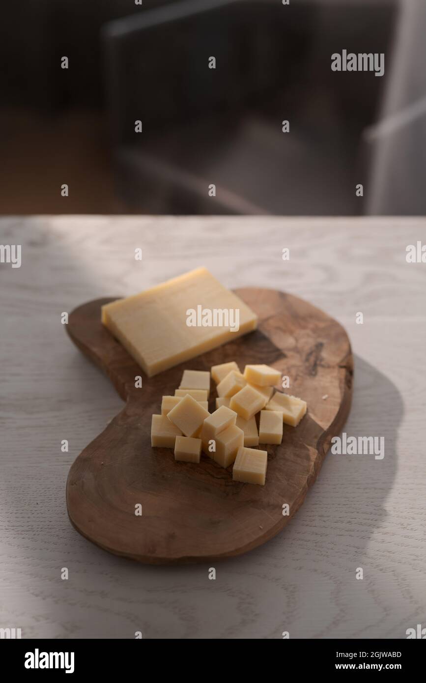 Small block of aged cheese sliced in small pieces on wood board ...