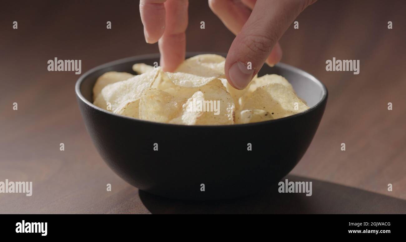 man hand take potato chips from black bowl on walnut table, wide photo ...