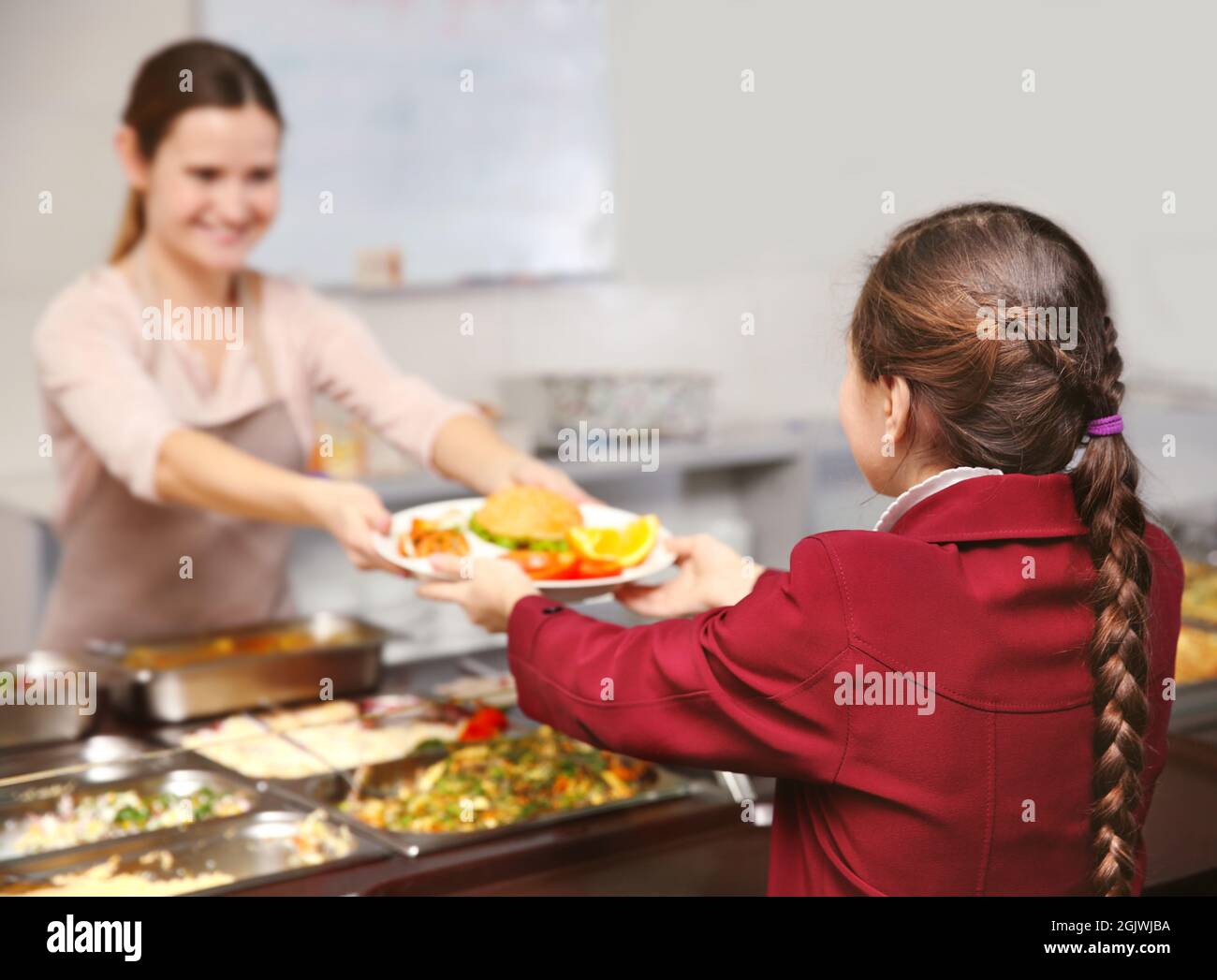 Pleasant woman giving lunch to school girl in cafeteria Stock Photo - Alamy
