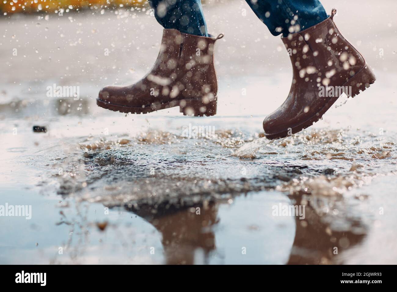 Woman wearing rain rubber boots walking running and jumping into puddle with water splash and ...