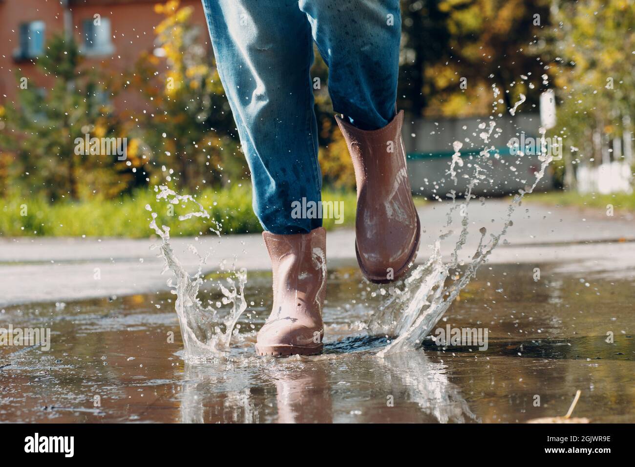 Woman wearing rain rubber boots walking running and jumping into puddle ...