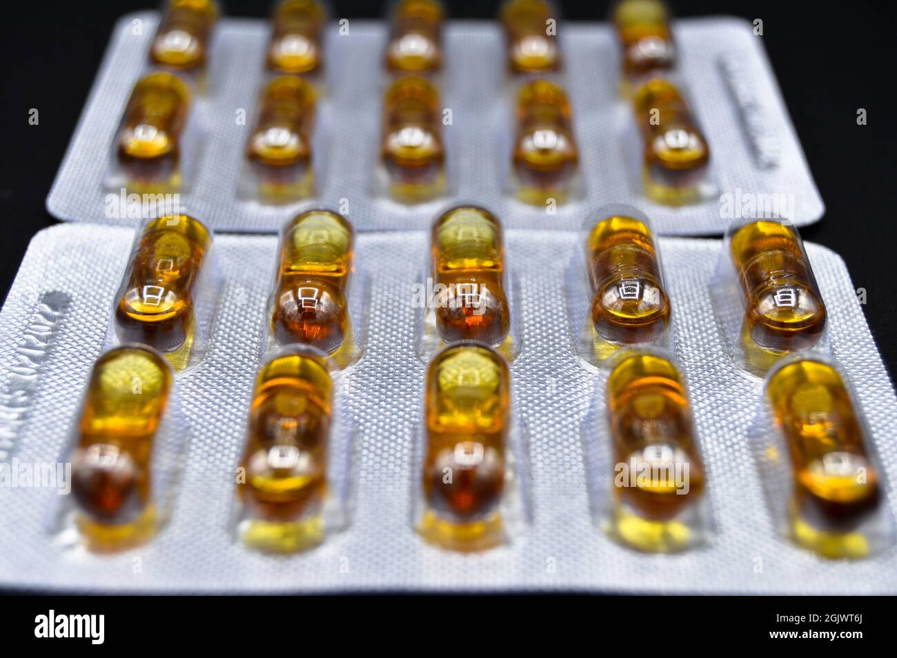 Yellow fish oil oval tablet pills packed, isolated on black background ...