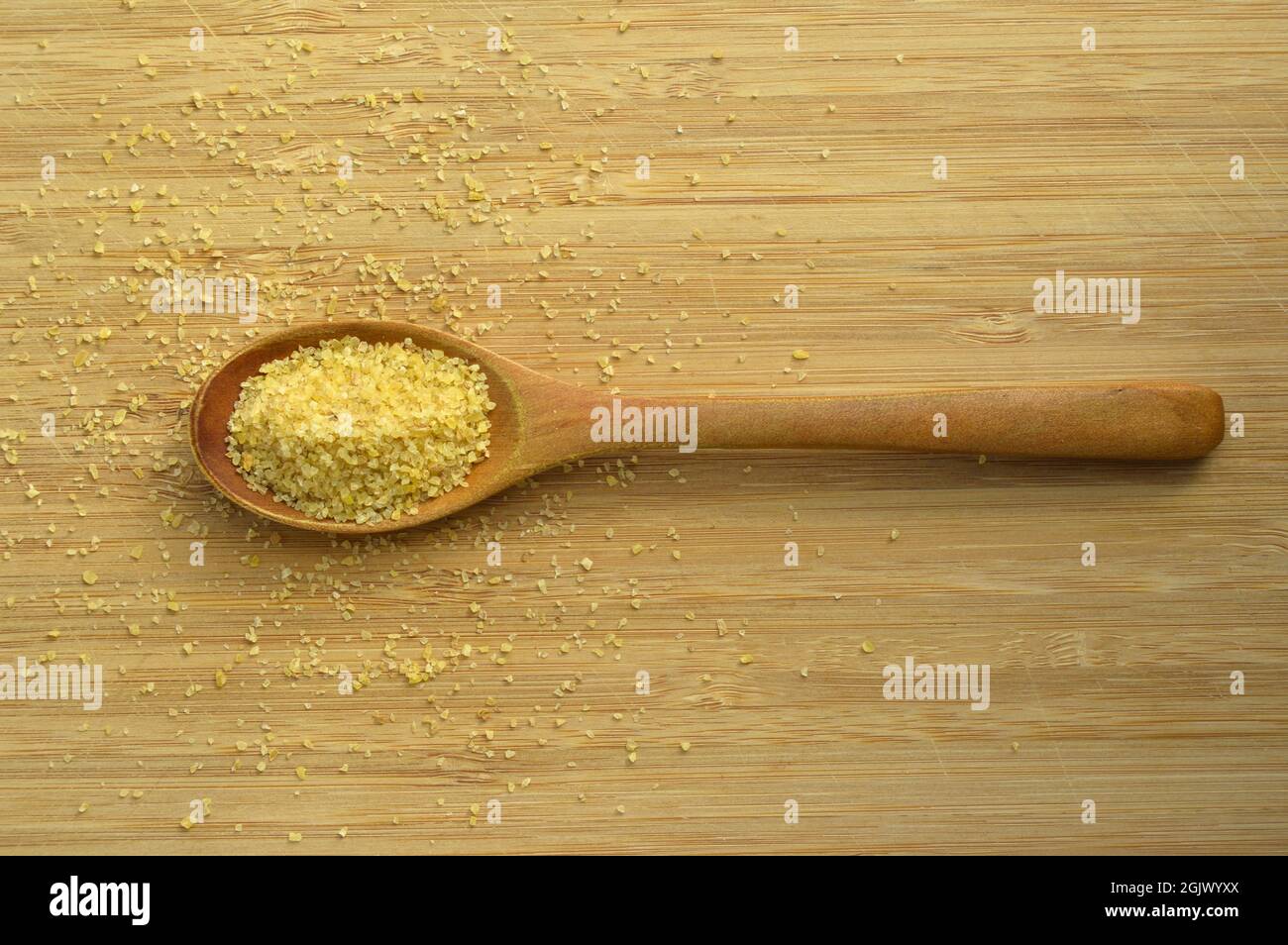 Dry cracked wheat daliya grains in wooden spoon, on bamboo cutting ...
