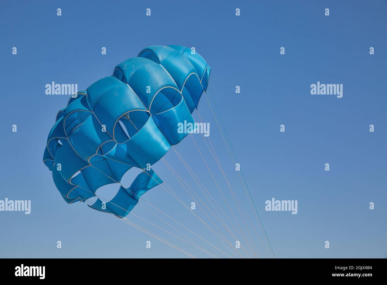Blue open parachute for paragliding watersports against clear blue sky ...