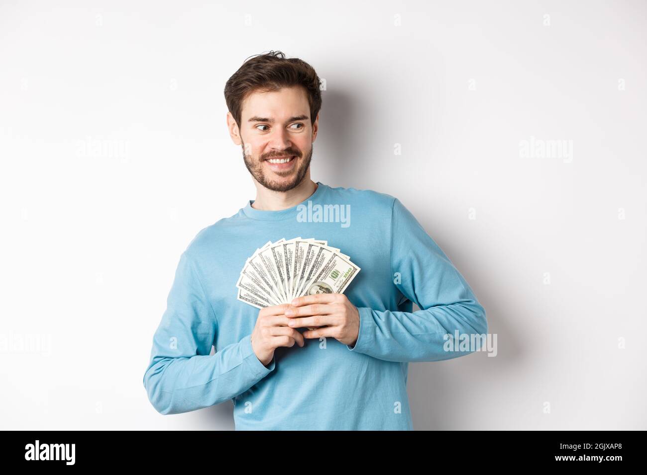 Greedy smiling man showing money and looking right, thinking about ...