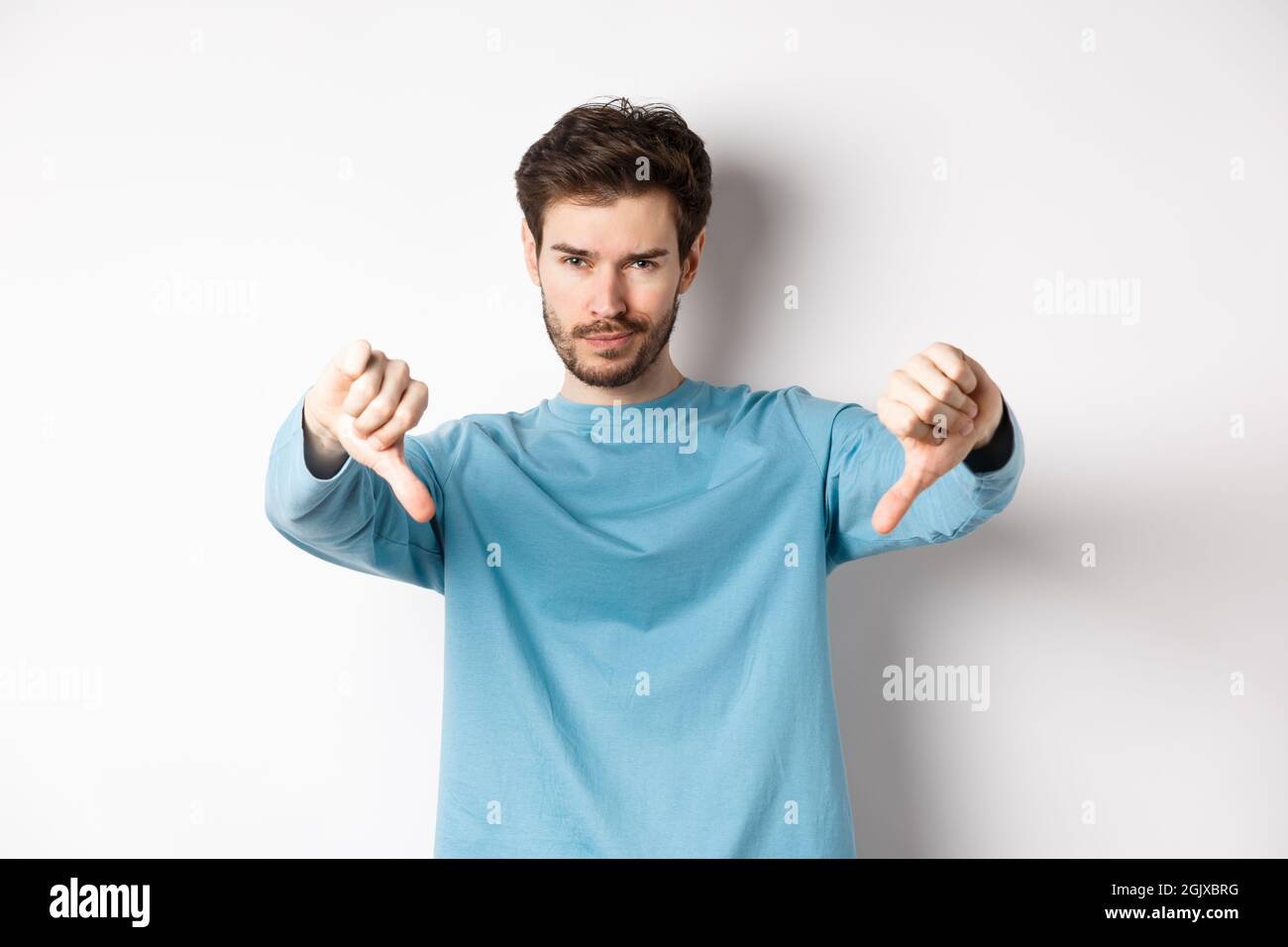 Skeptical handsome guy with beard, showing thumbs down in disapproval ...