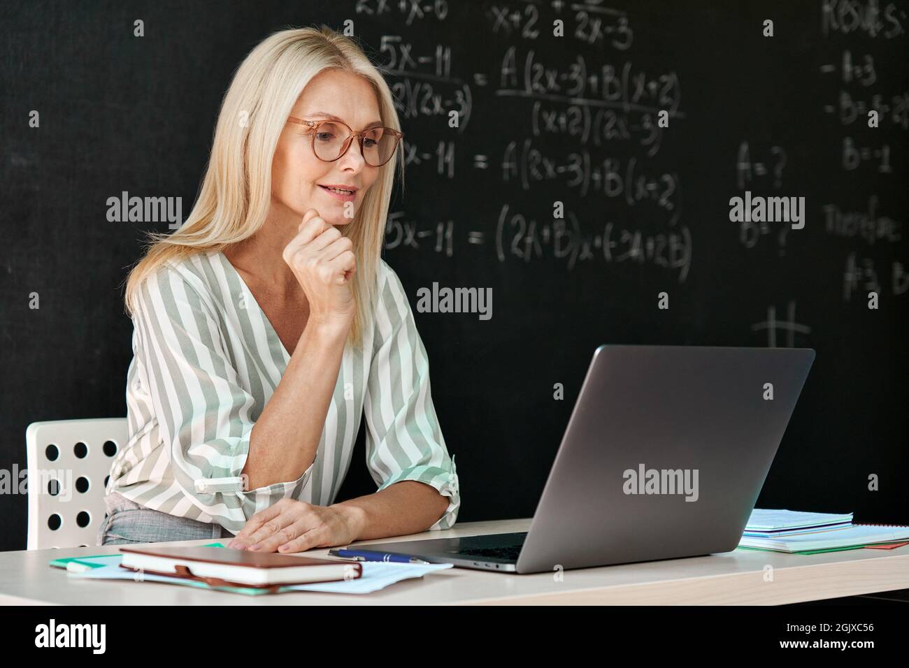 Happy teacher having online webinar maths lesson sitting at chalkboard ...