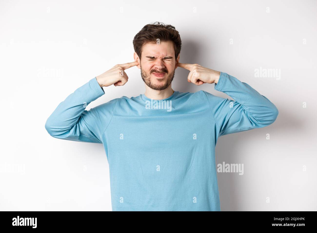 Annoyed young man plug ears from loud awful sound, being disturbed by ...