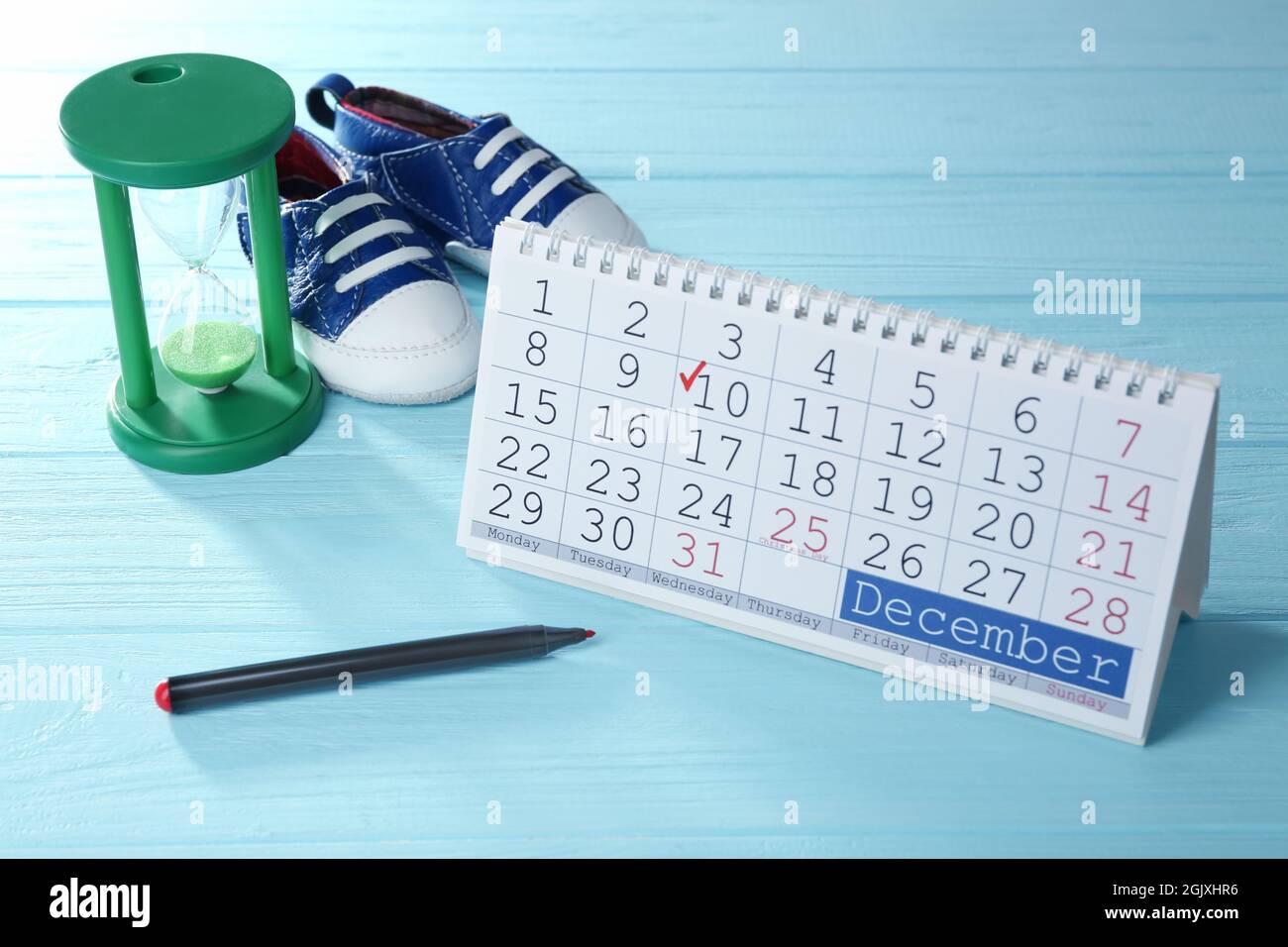 Calendar with marked date, marker, booties and hourglass on wooden ...