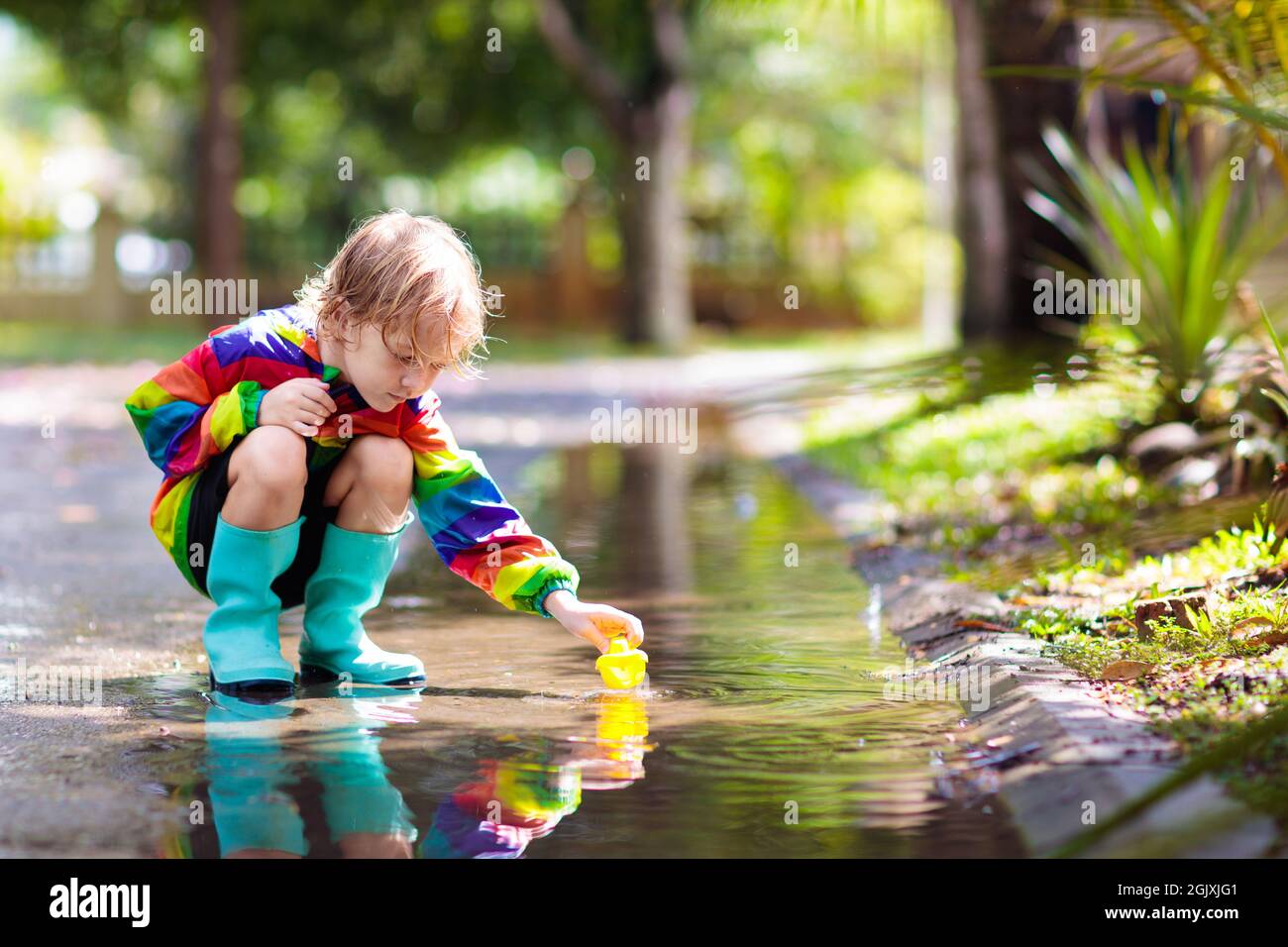Kid playing in the rain in autumn park. Child jumping in muddy puddle ...