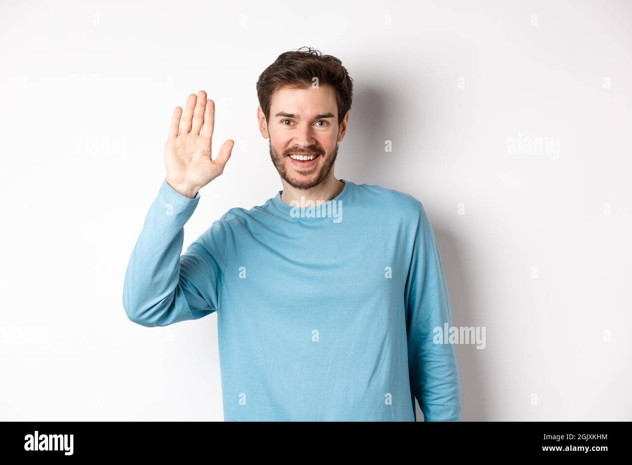 Cheerful young man with beard saying hello, looking friendly and waving ...