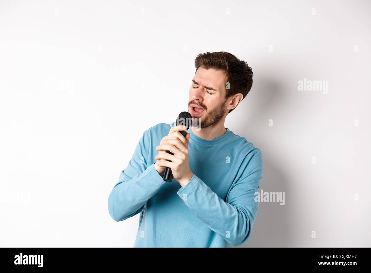 Romantic man singing song in microphone at karaoke, standing over white ...
