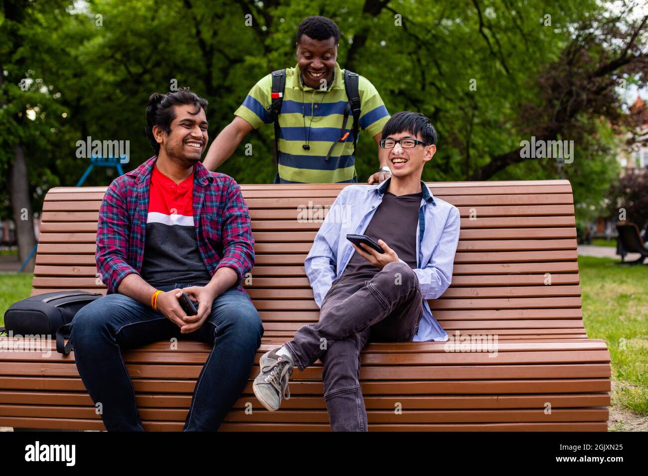 Three close cheerful diverse friends meeting on wooden bench at the ...
