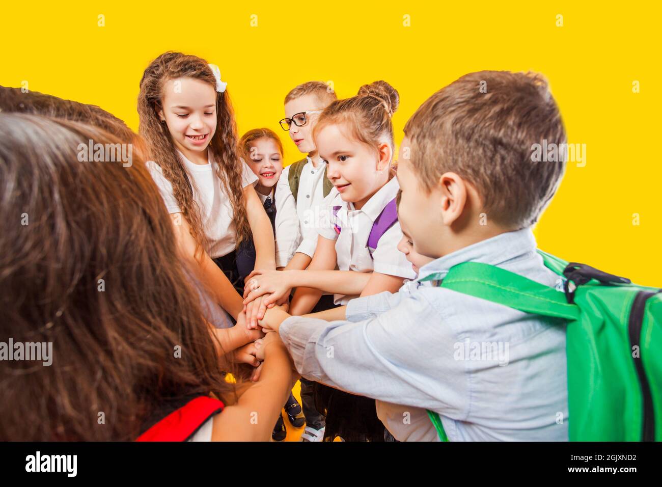 The schoolchildren are stacking hands together at the yellow background ...
