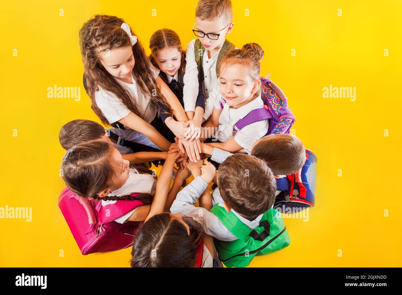 The schoolchildren are stacking hands together at the yellow background ...