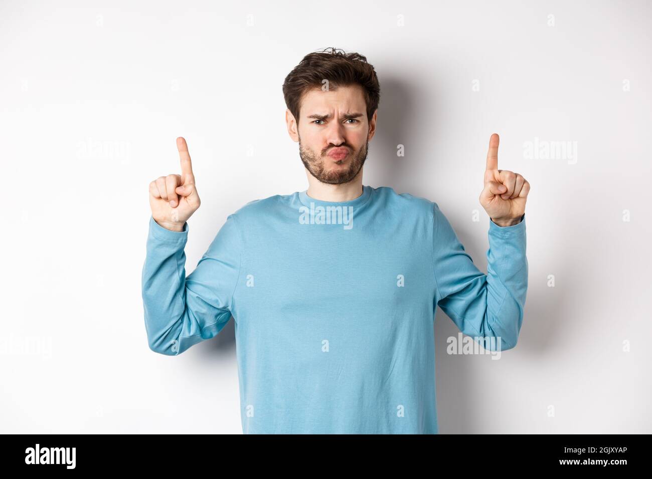Disappointed male model frowning and sulking, pointing fingers up with ...