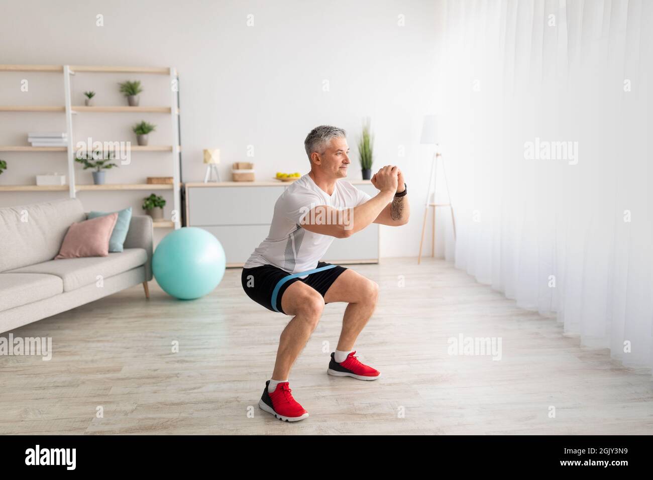 Morning training. Sporty mature man doing squats, exercising in living ...