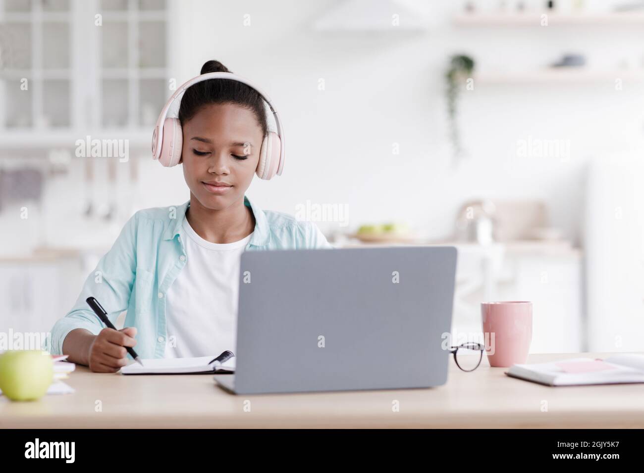 Happy busy teen black girl in earphones studying, doing homework at ...