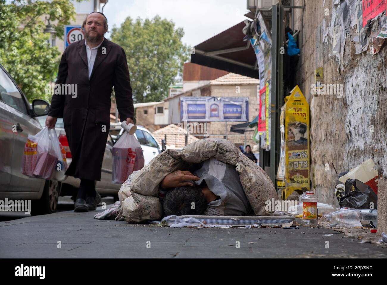 An orthodox Jew walks past a homeless person sleeping in the street in ...