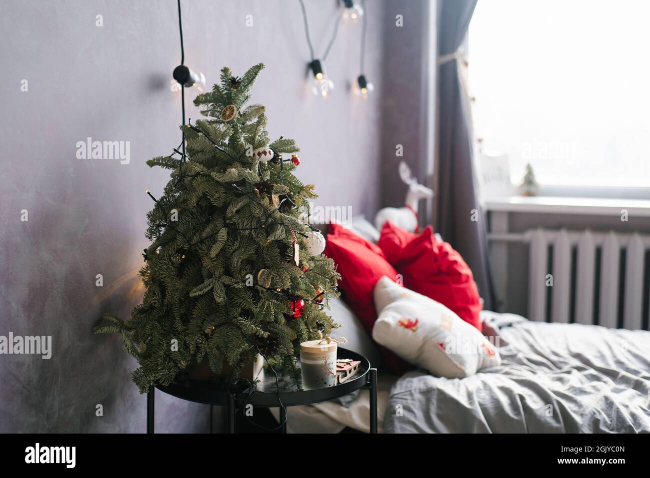 Small christmas tree on the bedside table and gifts near the bed in ...