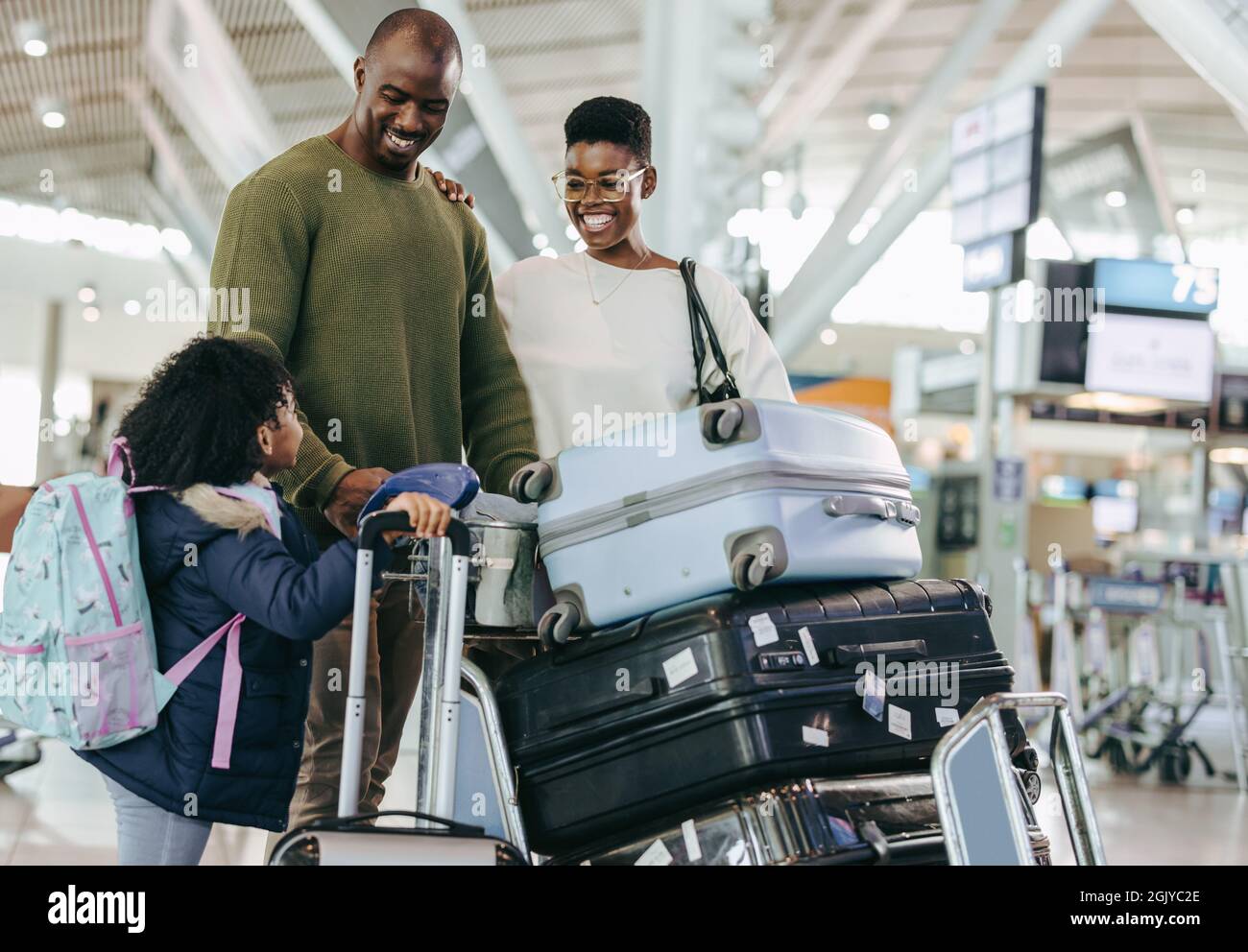 Happy parents and young daughter with luggage standing at airport ...