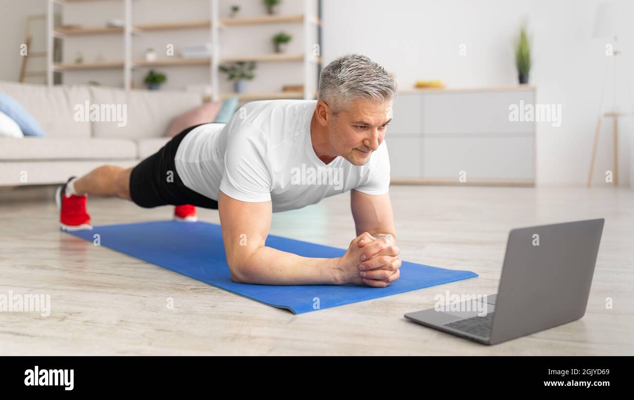 Happy mature man exercising and watching video on laptop computer ...