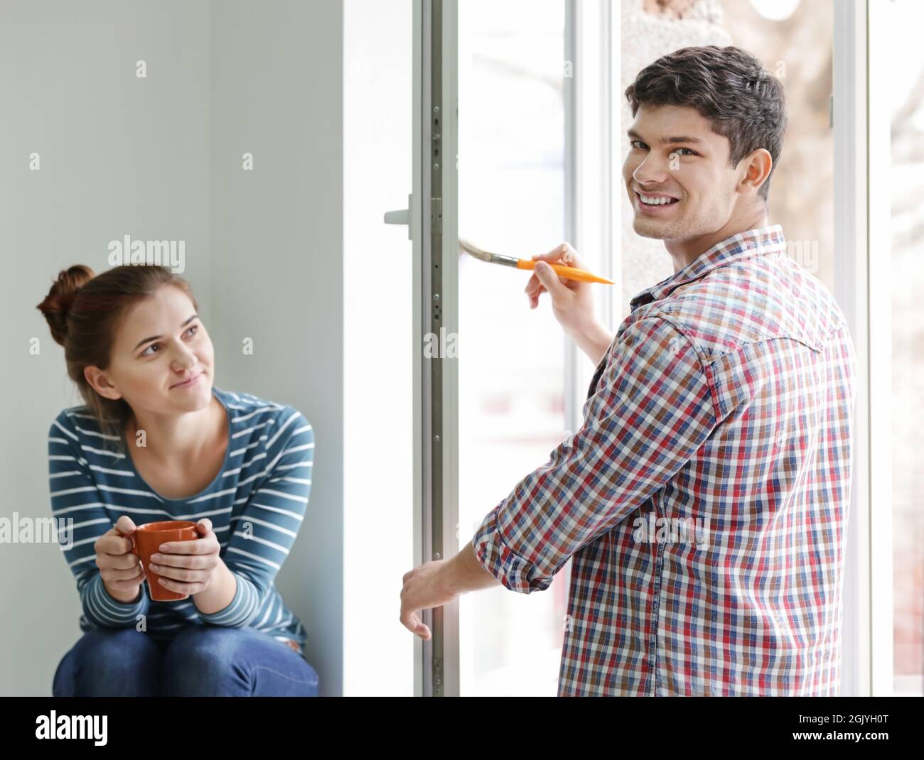 Handsome man painting window in young woman's apartment Stock Photo - Alamy