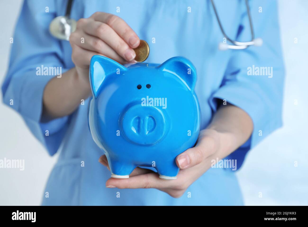 Female doctor putting coin into piggy bank, close up. Concept of ...