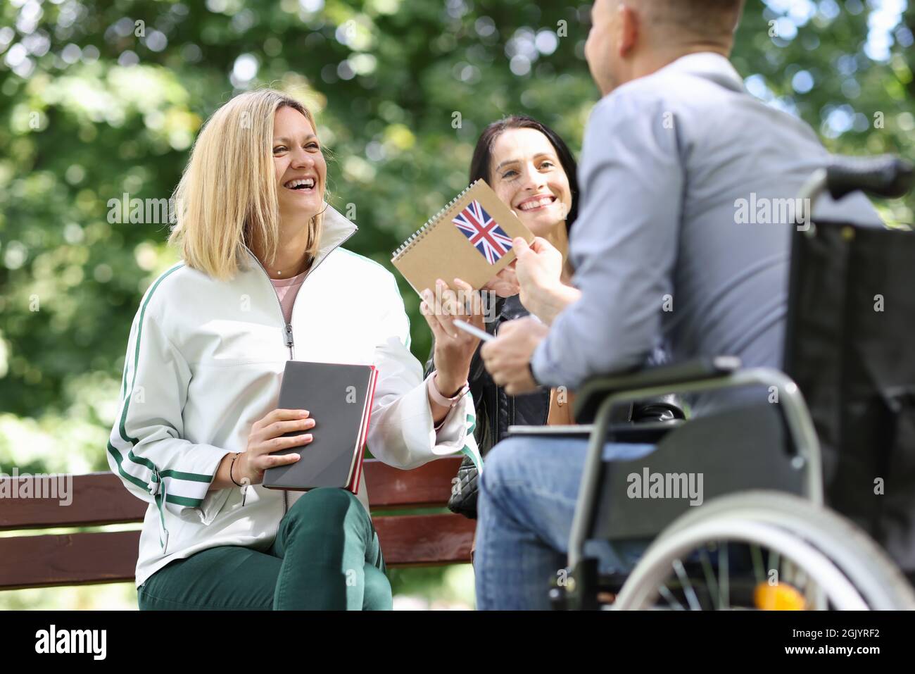 Disabled man in wheelchair giving english textbook to his female ...