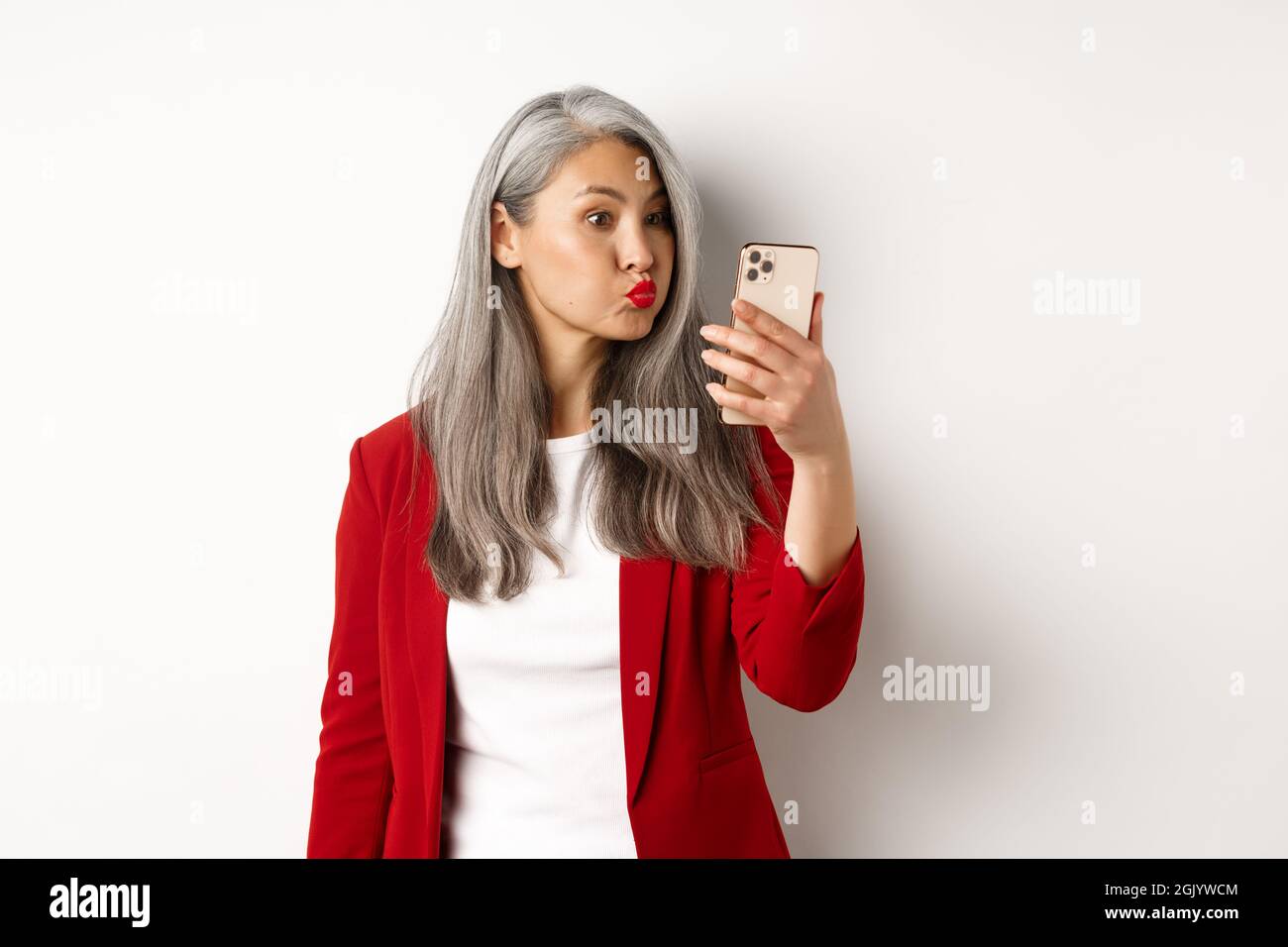 Silly and funny asian senior woman pouting, taking selfie on smartphone ...