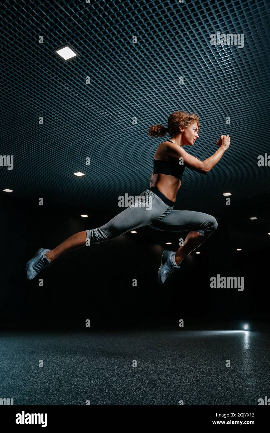 Woman jumps high in sports clothes on a black background of the gym ...