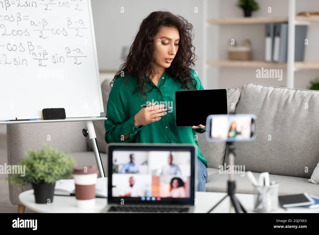 Female teacher explaining math online showing tablet to laptop Stock ...