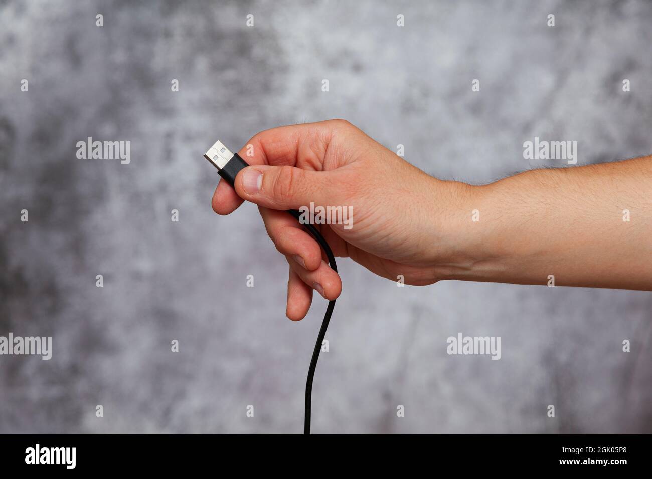 A man's right hand holding a black USB cable on a textured gray ...