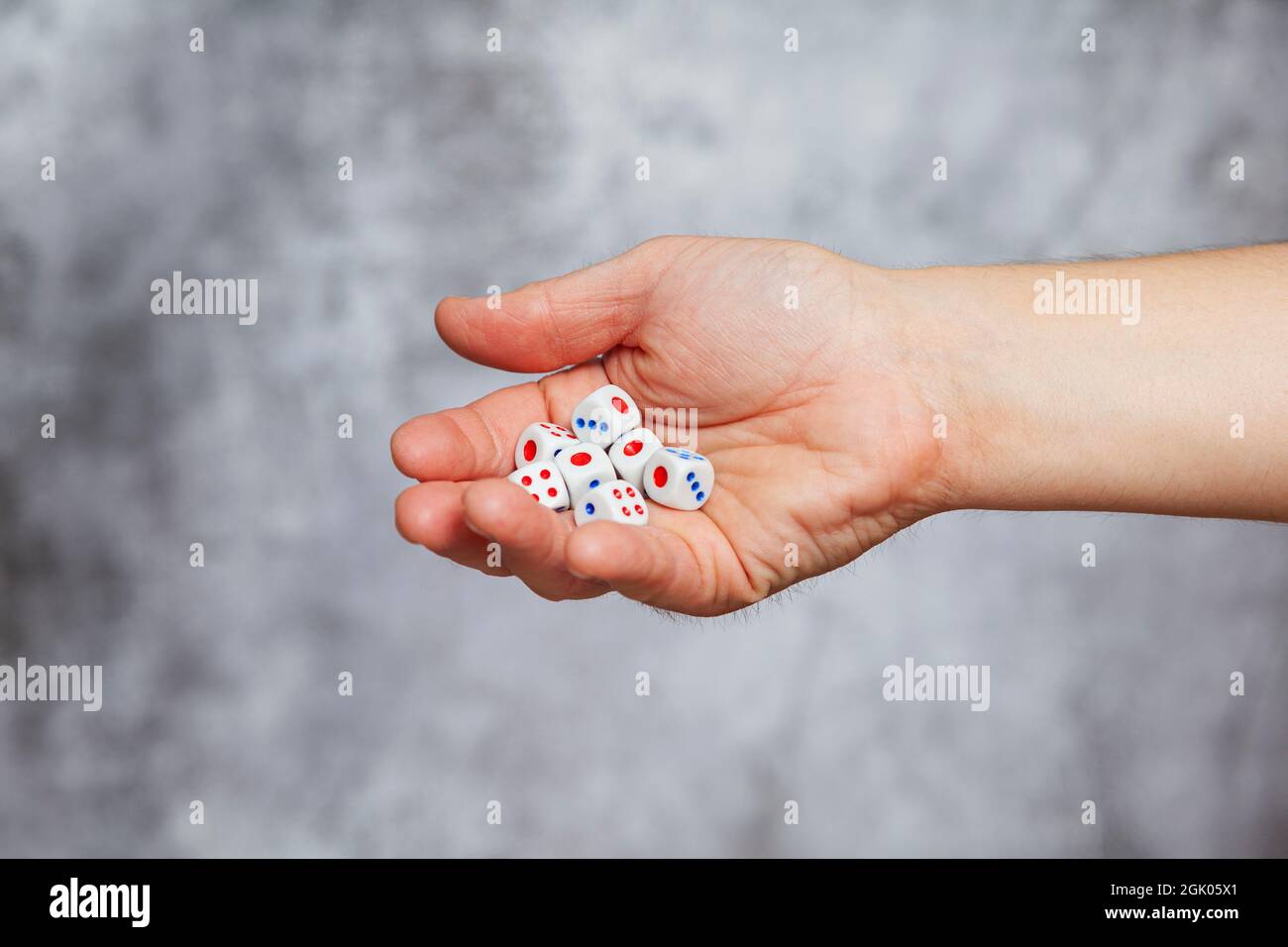 A man's right hand holding several white dice with red and blue dots on ...
