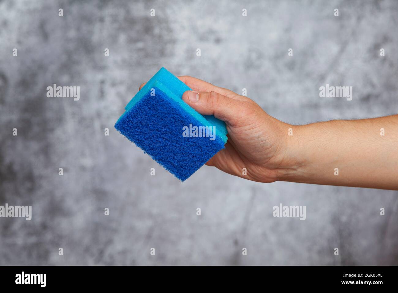 A man's right hand holding a blue scrubbing pad on a textured gray ...
