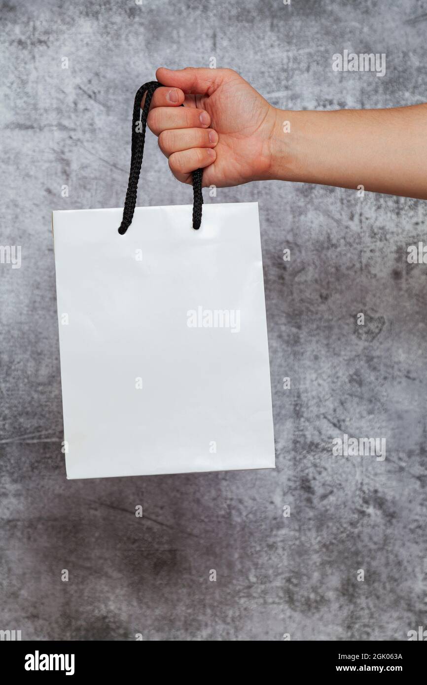 A man's right hand holding a white shopping bag with black rope handles ...