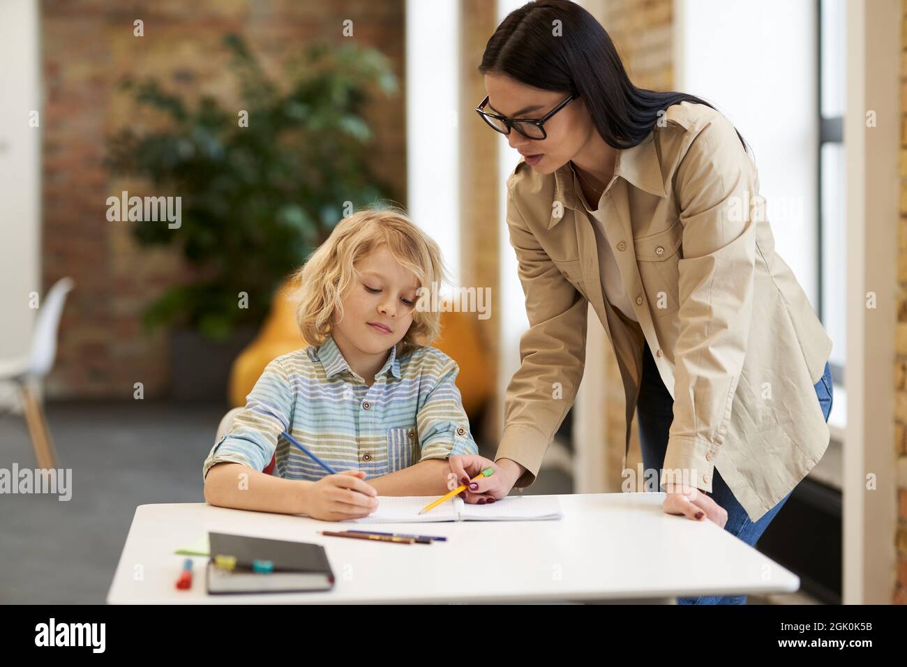 Supportive young female teacher in glasses helping little boy with the ...