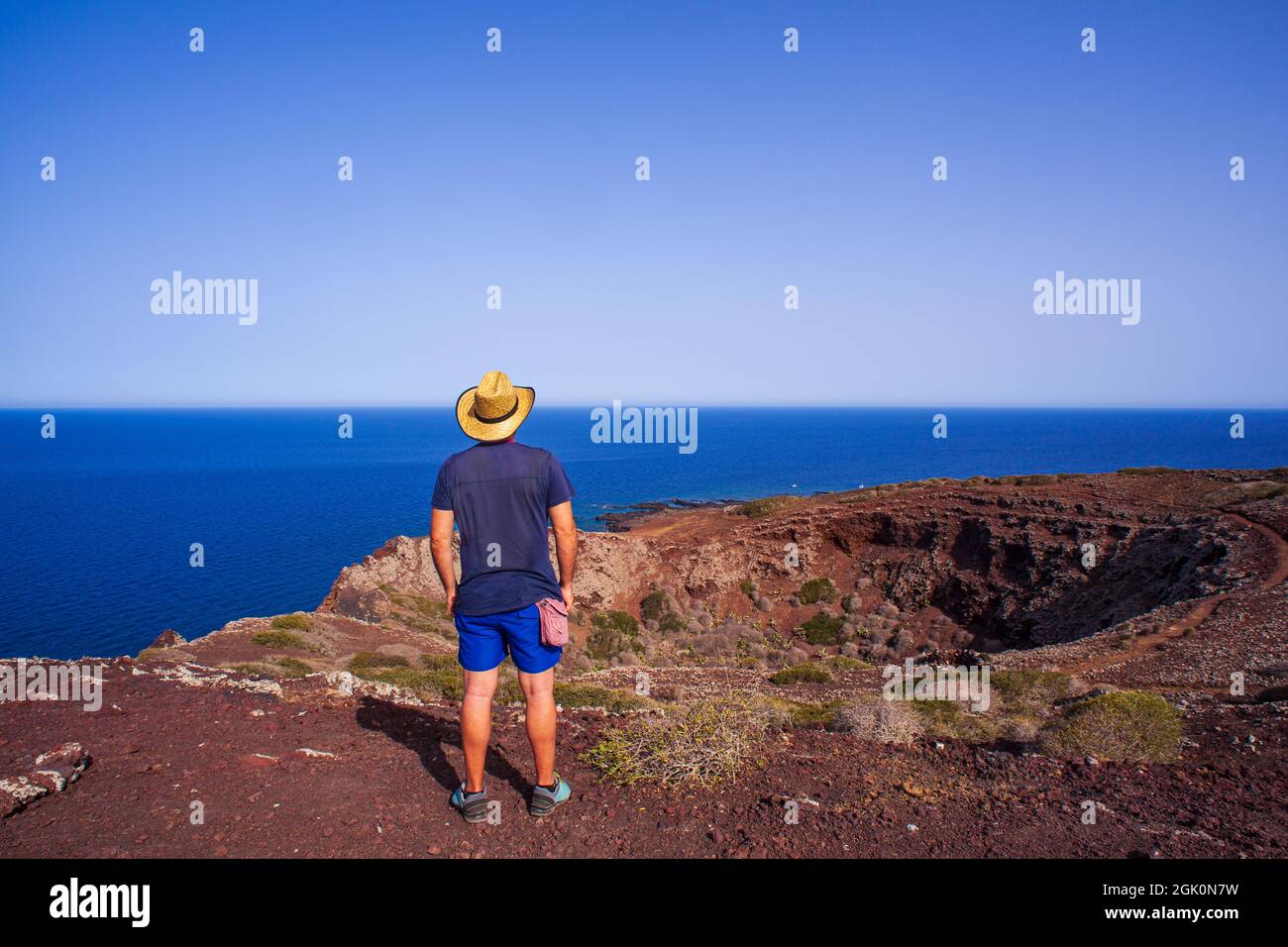 A man with a straw hat looking the sea from the top of the volcano ...