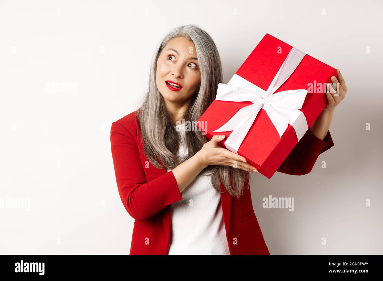 Elegant asian senior woman shaking gift box, trying to guess what ...