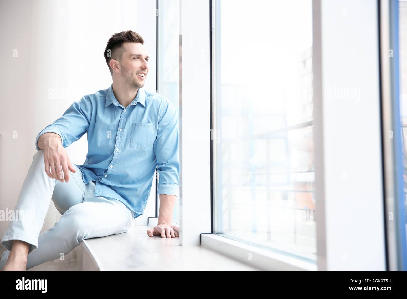 Smiling man sitting on sill near big white plastic window Stock Photo ...