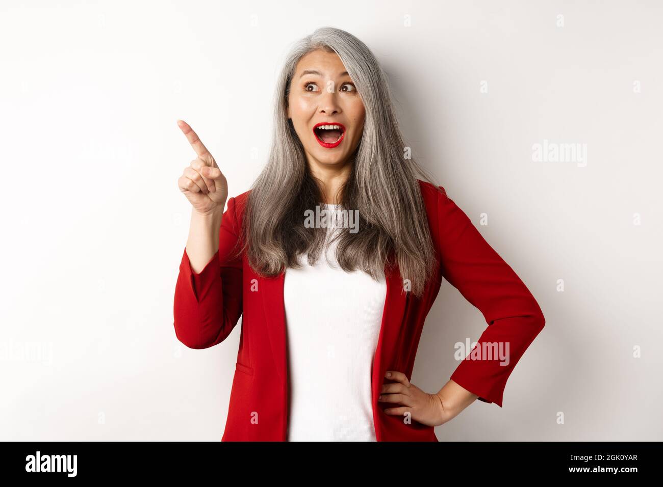 Surprised senior asian lady pointing upper left corner, checking out ...