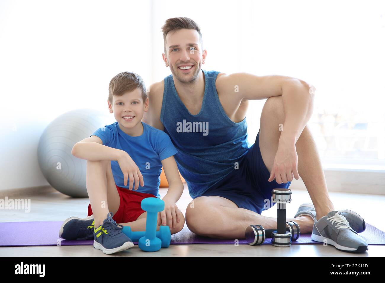 Dad and son sitting on floor with dumbbells in gym Stock Photo - Alamy