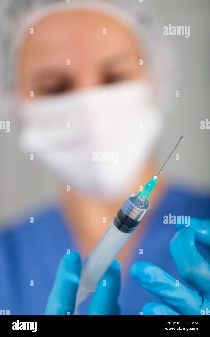 Experienced masked nurse prepared a syringe for injection, filling it ...
