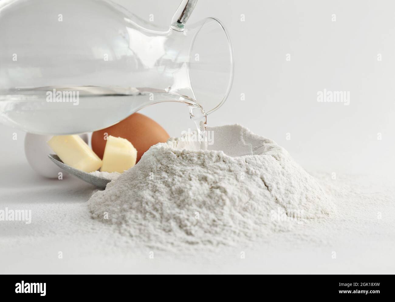 Pouring water into heap of flour on white background Stock Photo - Alamy
