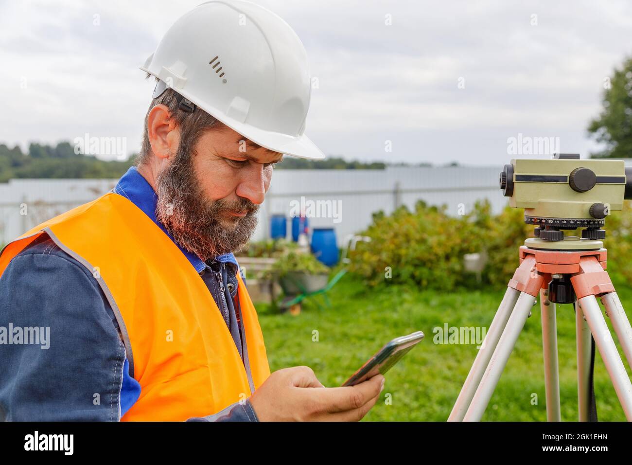 A civil engineer with an optical level looks into a mobile phone. A ...